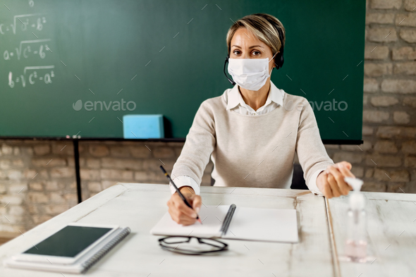 School teacher wearing face mask and holding online lecture form the ...