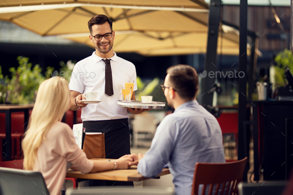 Happy waiter serving guests in an outdoor cafe. Stock Photo by drazenphoto
