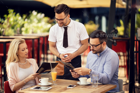 Happy waiter talking to a couple while they are reading menu in a ...