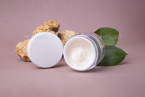 Open cosmetics container with white cream and glossy green leafs on ...