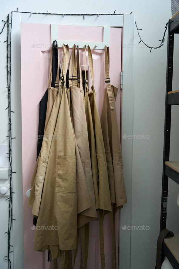 Work aprons hang on a hanger in the workshop Stock Photo by svitlanah