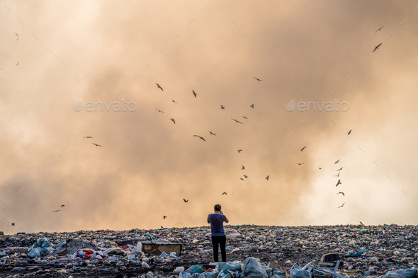 Person standing on a landfill full of garbage and burning garbage piles ...