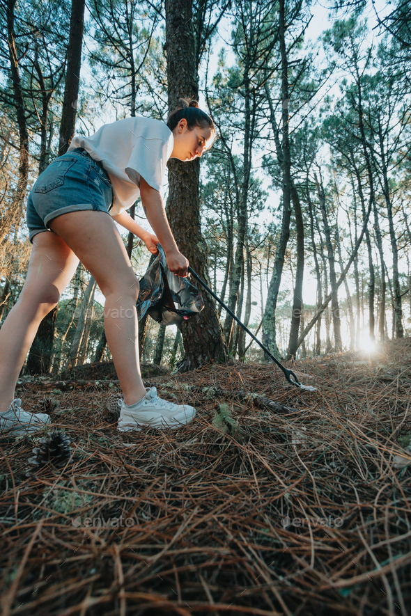 Photo of side of girl picking up garbage in bag on the forest during a ...