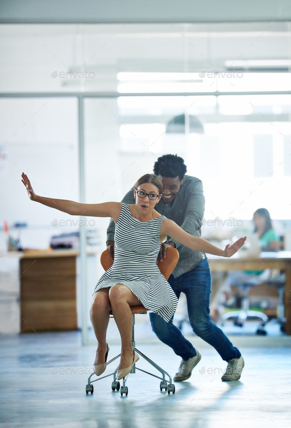 Shot of a male coworker pushing his female coworker around an office in ...