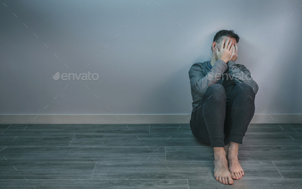 Man crying while covering his face with hands sitting on the floor ...