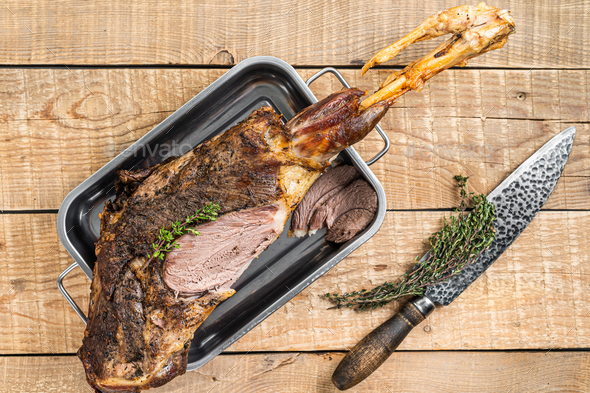 Whole oven roasted goat leg meat with thyme in a steel tray. Wooden ...