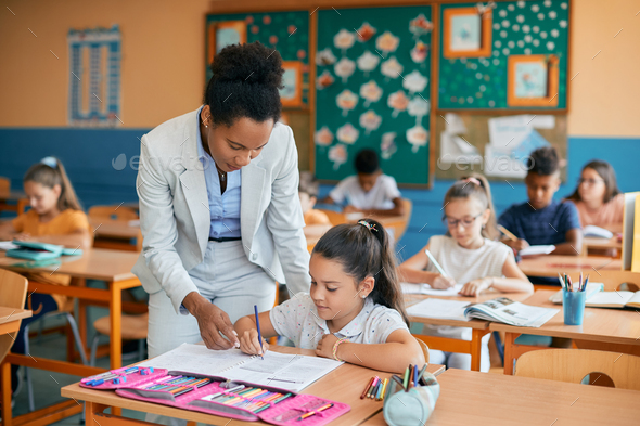 Black elementary school teacher assisting her student on a class in the ...