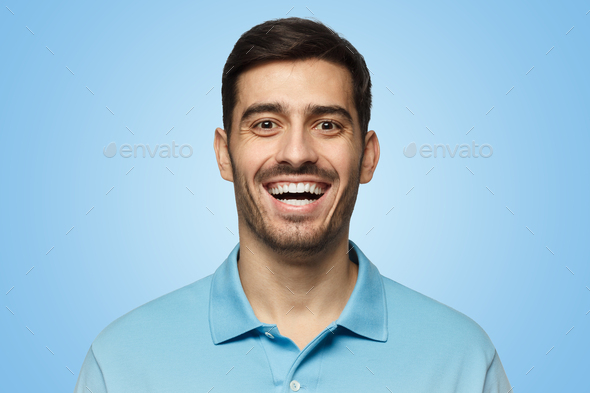 Handsome young man in blue polo shirt smiles broadly, laughing, showing ...