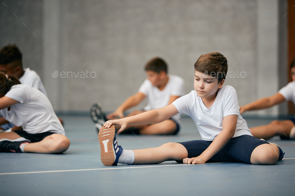 Elementary student stretching on the floor during PE class at school ...