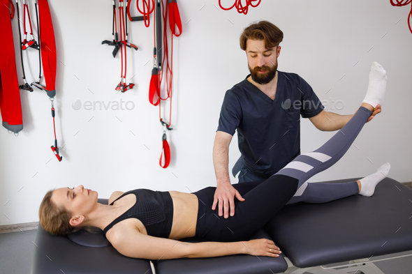 Professional physiotherapist lifting his female patients leg. Doctor ...