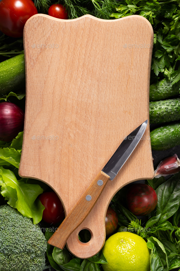 Variety of fresh vegetables and wood cutting board at table background ...