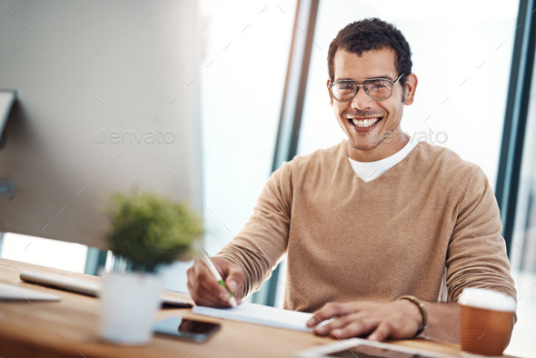 Portrait of a young designer writing notes while working at his desk in ...