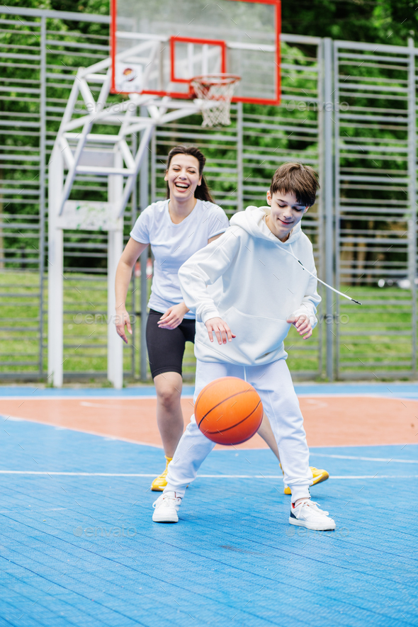 Girl and her younger brother, teenager, play basketball on modern ...