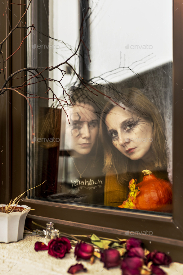 Two witches look through out of the window of Halloween decorations ...