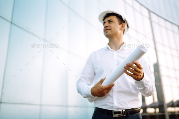Young worker in a helmet and with a phone at a work object. Business ...