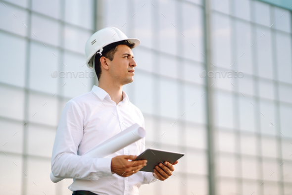 Young worker in a helmet and with a phone at a work object. Business ...