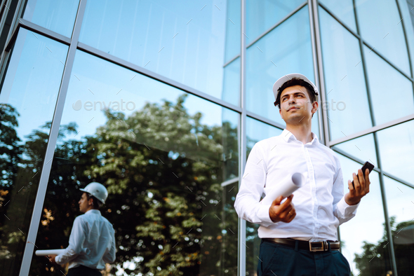 Young worker in a helmet and with a phone at a work object. Business ...