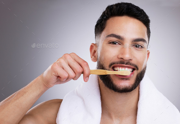 Shot of a handsome young man brushing his teeth against a studio ...