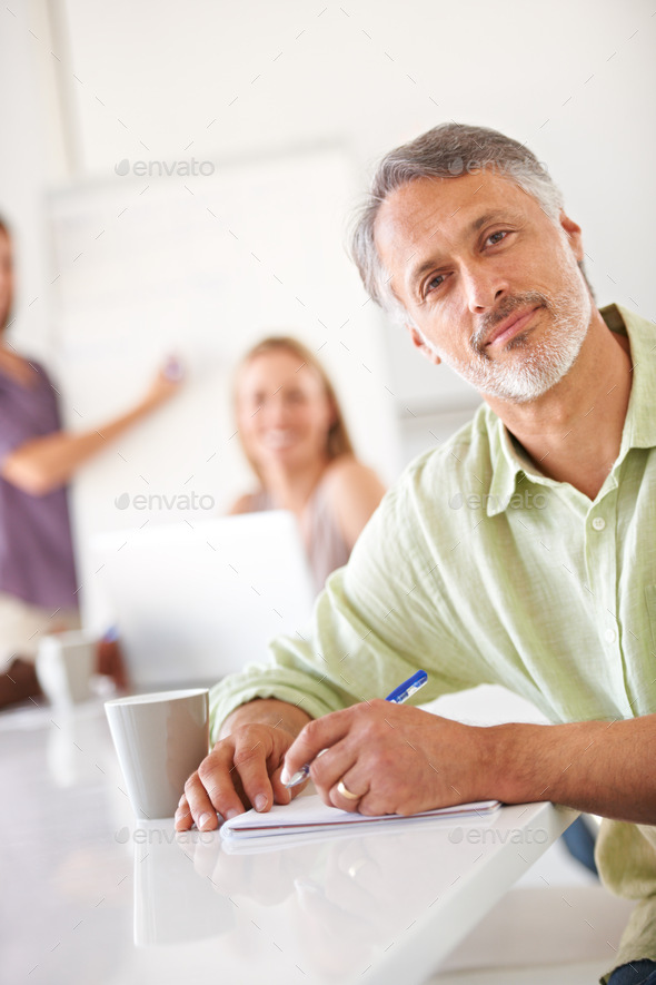 Handsome mature businessman looking composed with his coworkers blurred ...