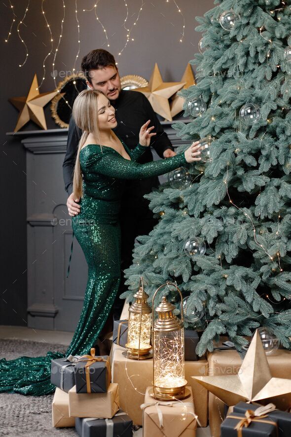 Romantic couple standing near Christmas tree wearing magnificent ...