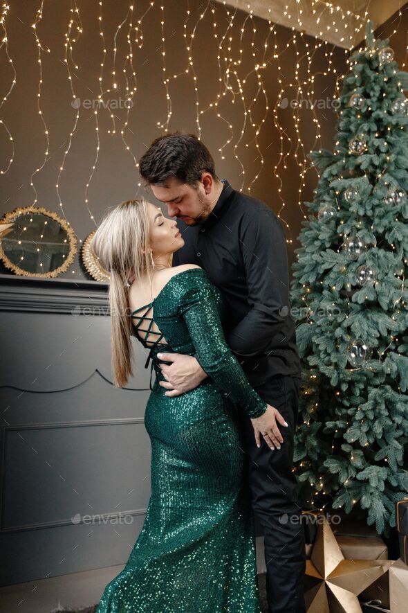 Romantic couple standing near Christmas tree wearing magnificent ...