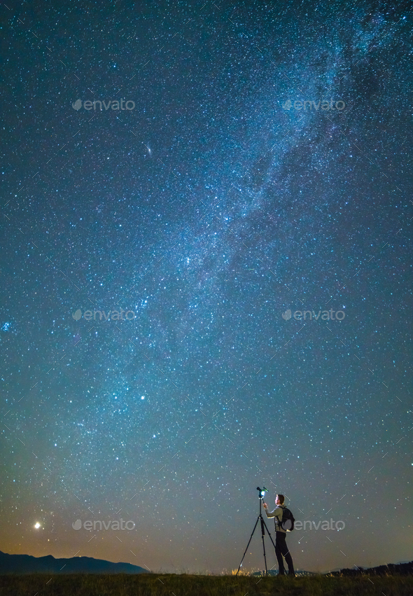 The man with a camera stand on the starry sky background. night time ...