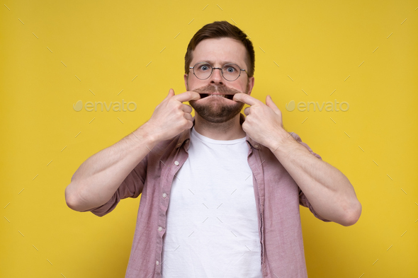 Whimsical man in glasses made a frightening grimace, he put fingers in ...