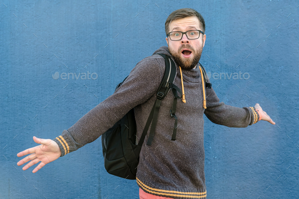 Carefree man with an urban backpack, with an innocent look, shrugs and ...