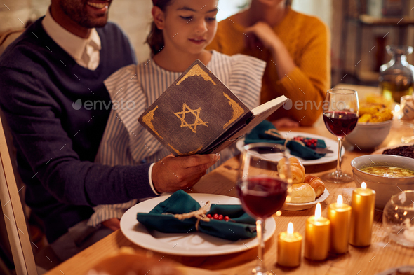 Close-up of family reading Hebrew bible during Hanukkah meal at dining ...