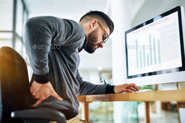 Shot of a young designer suffering from back pain while working at his ...
