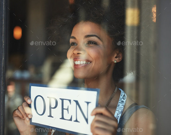 Shot of a young woman hanging up an open sign on the window of her cafe ...