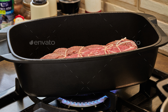 Piece of beef meat being fried in rectangular cooking pot over fire on ...