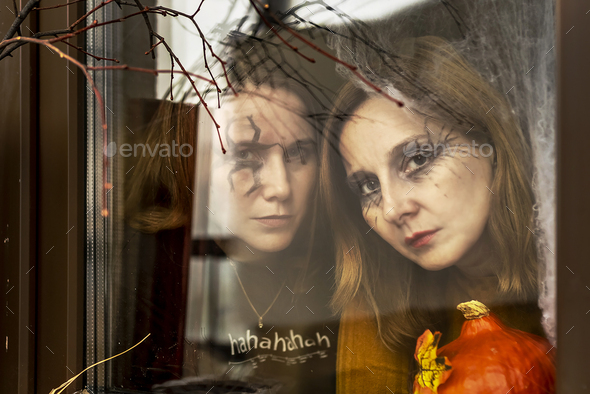 Two witches look through of the window of Halloween decorations ...