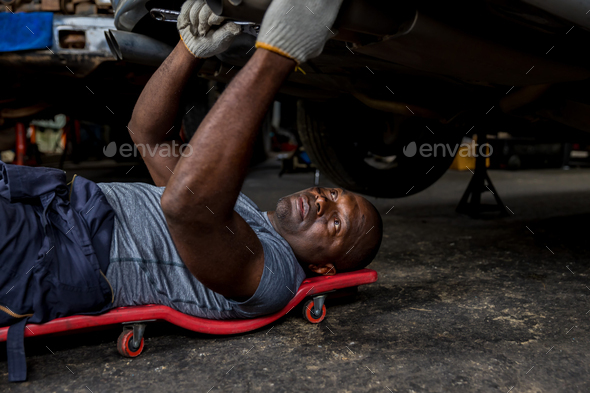 Mechanic lying down and working under car at auto service garage. Stock ...