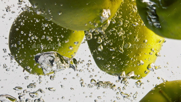 Whole apples falling water closeup. Green sour fruits flow in light ...
