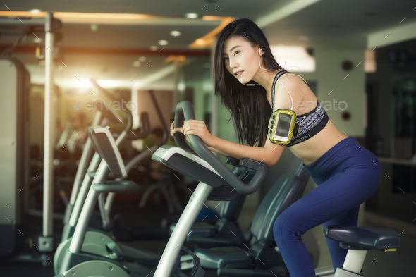 Happy woman riding an exercise bike in gym Stock Photo by FamilyStock