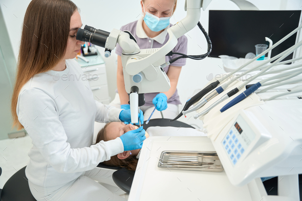 Dentist inspecting young patient oral cavity with modern diagnostic ...