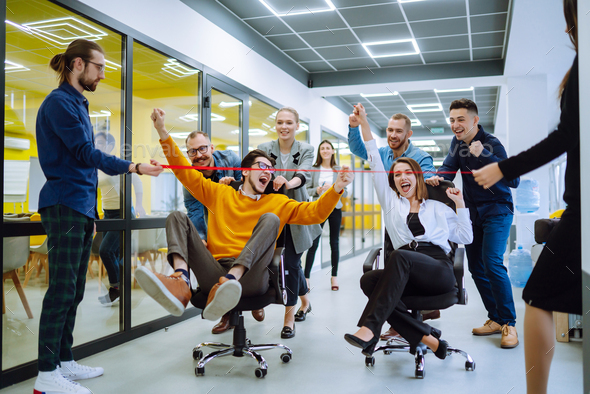 Young colleagues group having fun together, riding on chairs in office ...