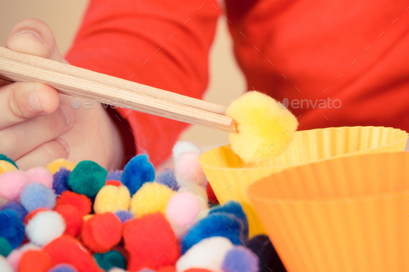 Preschooler playing with pompoms, wooden tongs and cups. Development of ...