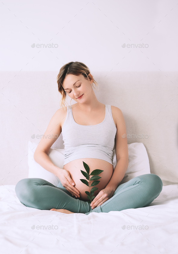 Pregnant woman holds green sprout plant near her belly as symbol of new ...