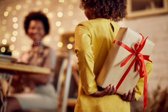 Back view of black little girl surprising her mother with Christmas ...