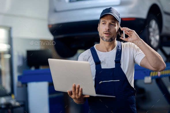Auto repairman talking on the phone while using laptop in a workshop ...
