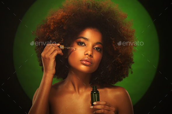 African girl applying serum to her face with dropper like skin care ...