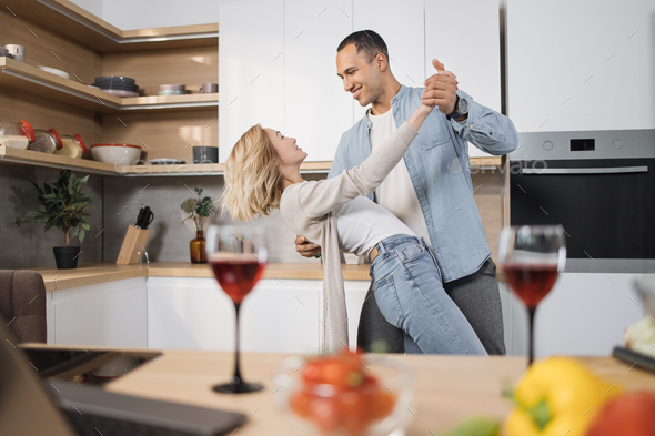 Smiling young man embracing and leaning woman during dancing on kitchen ...