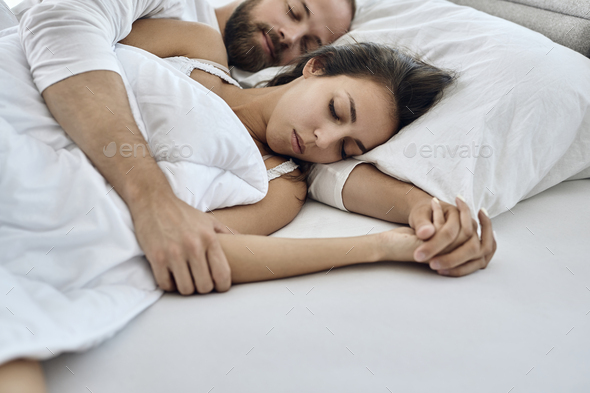 Loving couple holding hands while napping on a bed. Stock Photo by ...