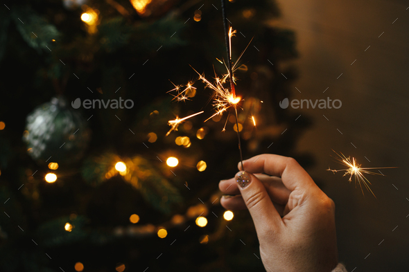 Hand holding firework against christmas tree lights in dark room. Happy ...