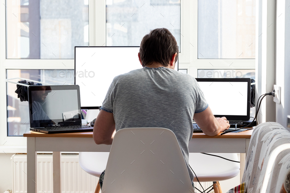 Man at workplace with two laptops and monitor near the window. Remote ...