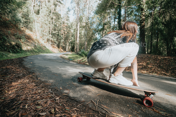 Sporty woman riding on the skateboard on the forest road. Longboarding ...