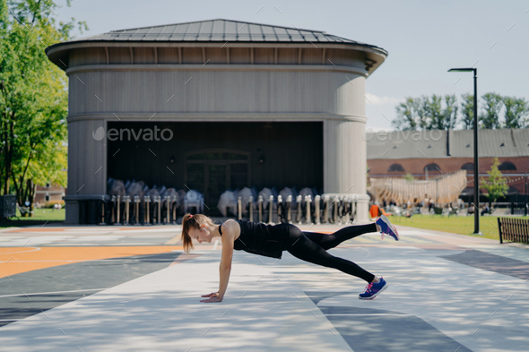 Sportive young woman being in good physical shape poses in plank raises ...