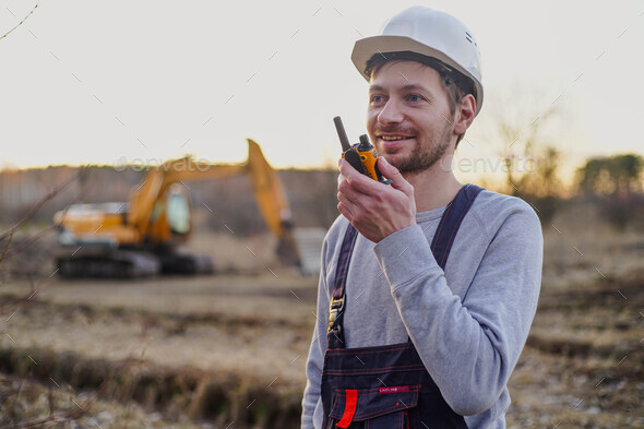 Smiling builder talking by radio transmitter on construction site ...
